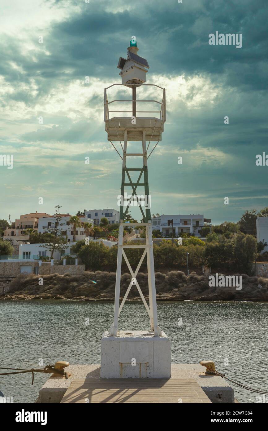 Small lighthouse at the edge of jetty with blue beacon on top. Village ...