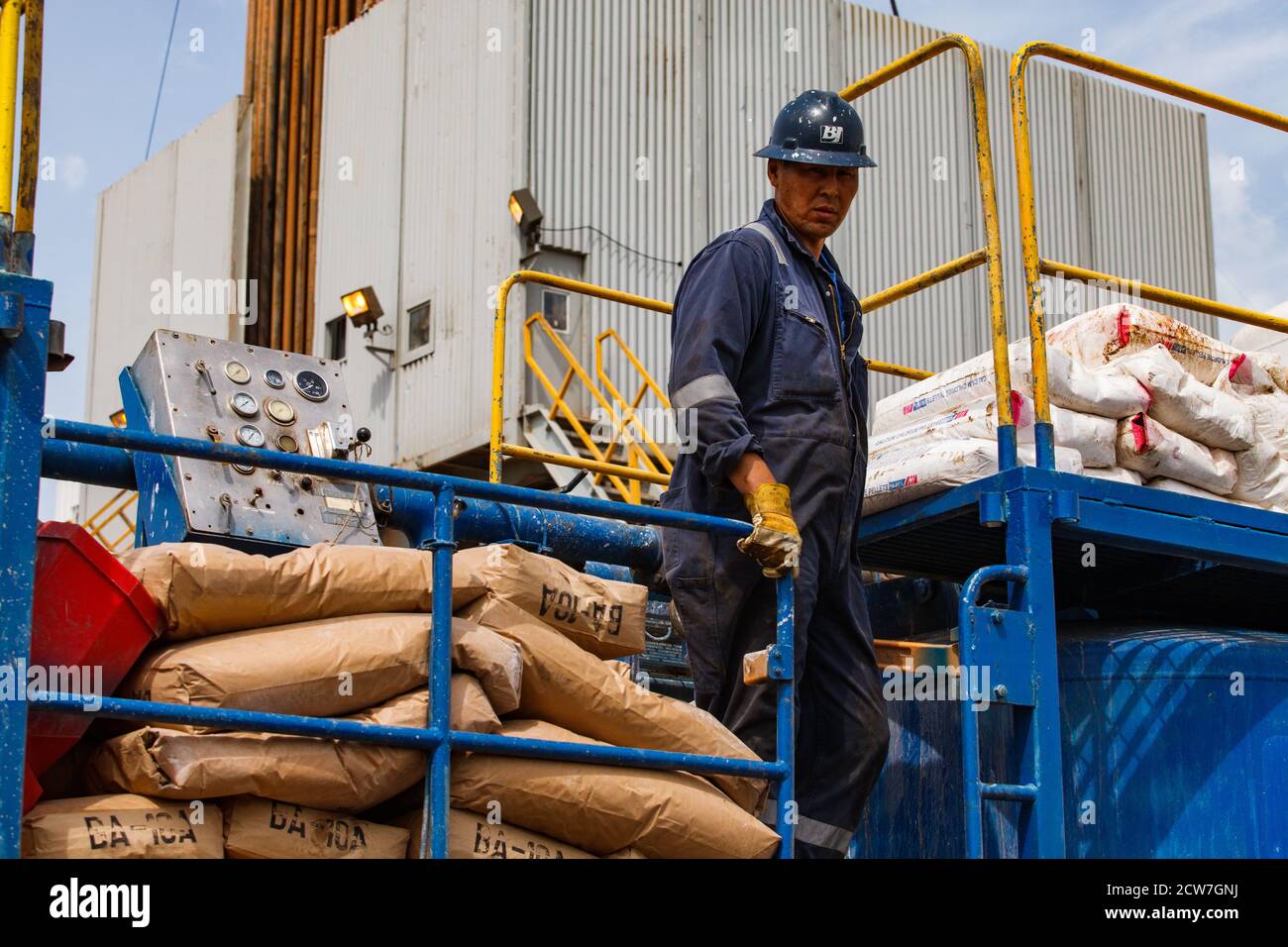 Oil deposit Zhaikmunai in desert. Worker in blue work wear and helmet ...