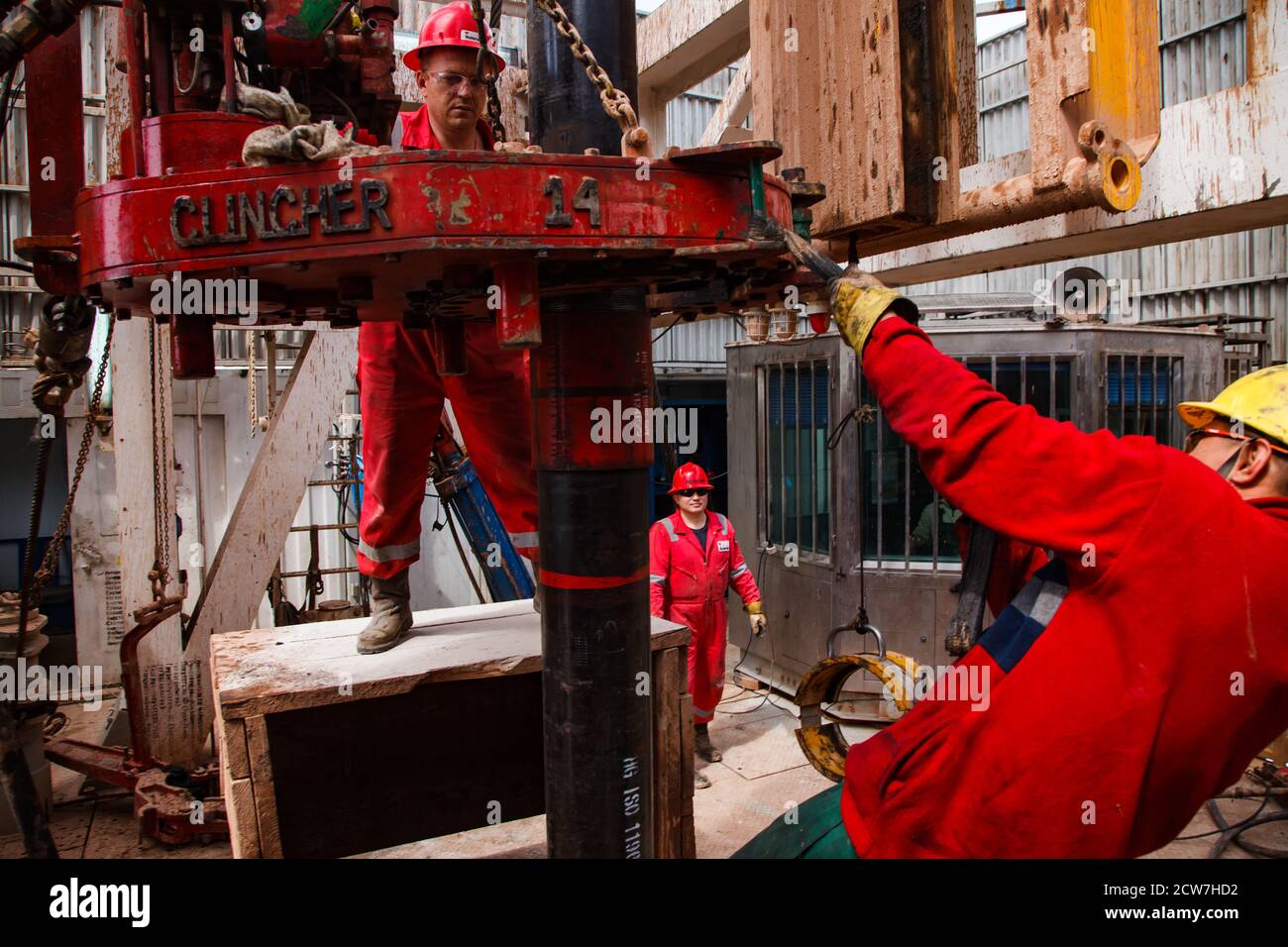 Workers with electric clincher tool on drilling rig. Red work wear ...