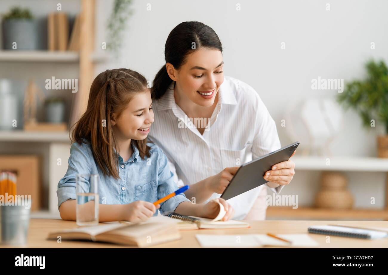 Back to school. Happy child and adult are sitting at desk. Girl doing ...