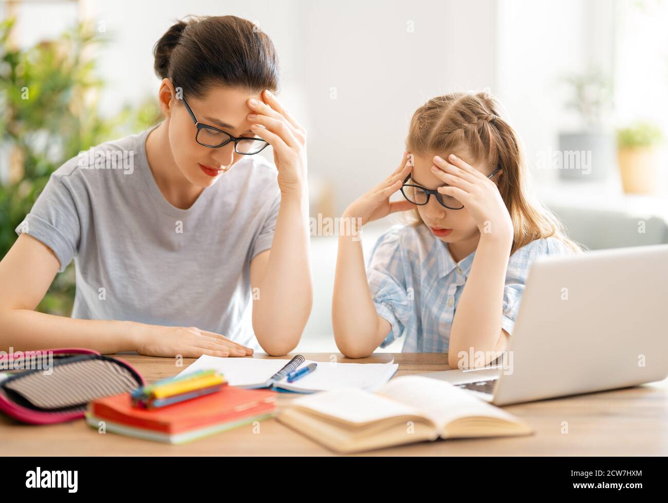 Back to school. Unhappy child and adult are sitting at desk. Girl doing ...