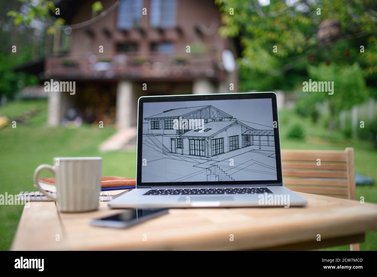 Laptop with blueprints on desk outdoors in garden, home office concept ...
