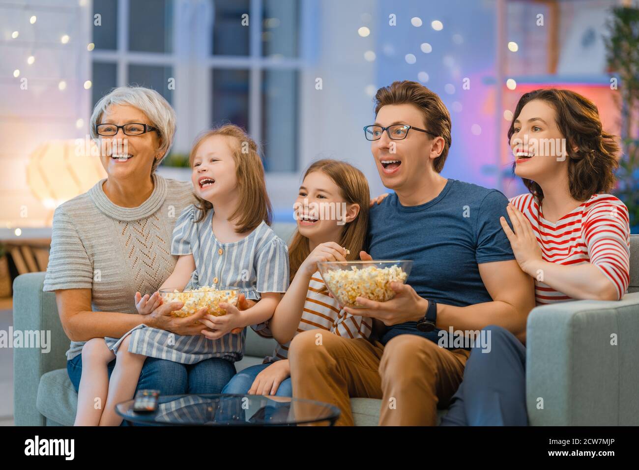 Happy family watching projector, TV, movies with popcorn in the evening ...
