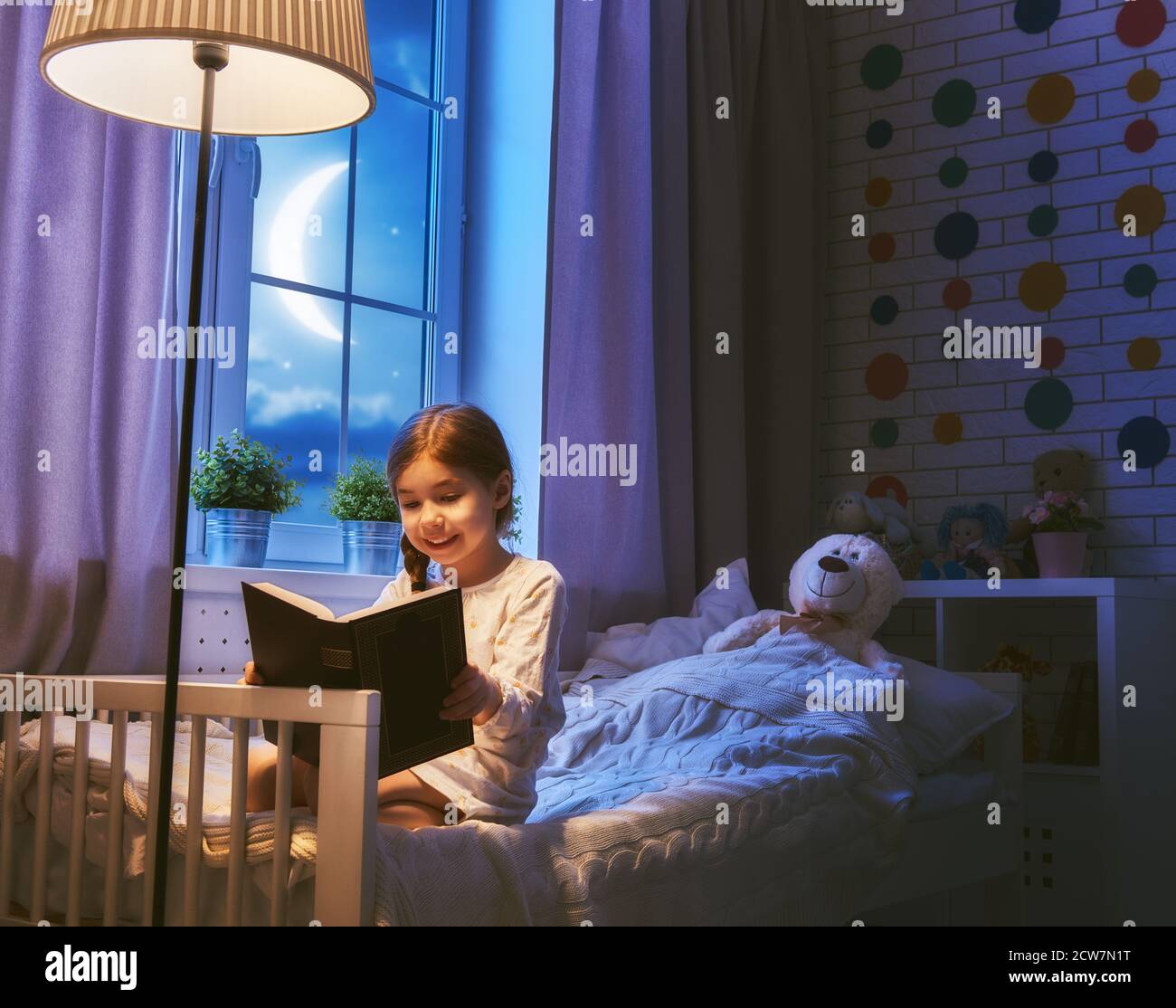 Cute little child girl reading a book under a lamp. Kid girl sitting in ...