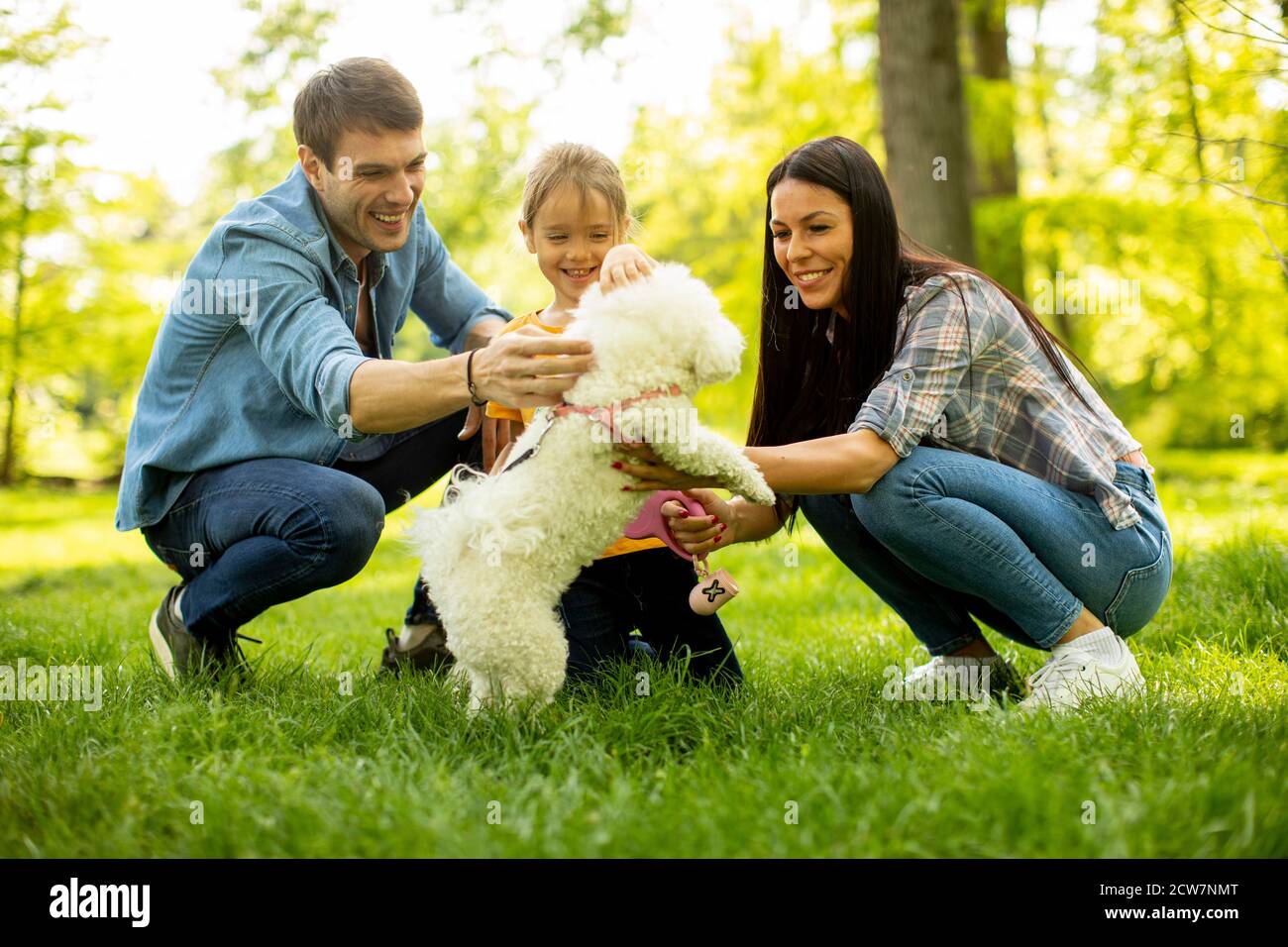 Beautiful happy family is having fun with bichon dog outdoors in the ...
