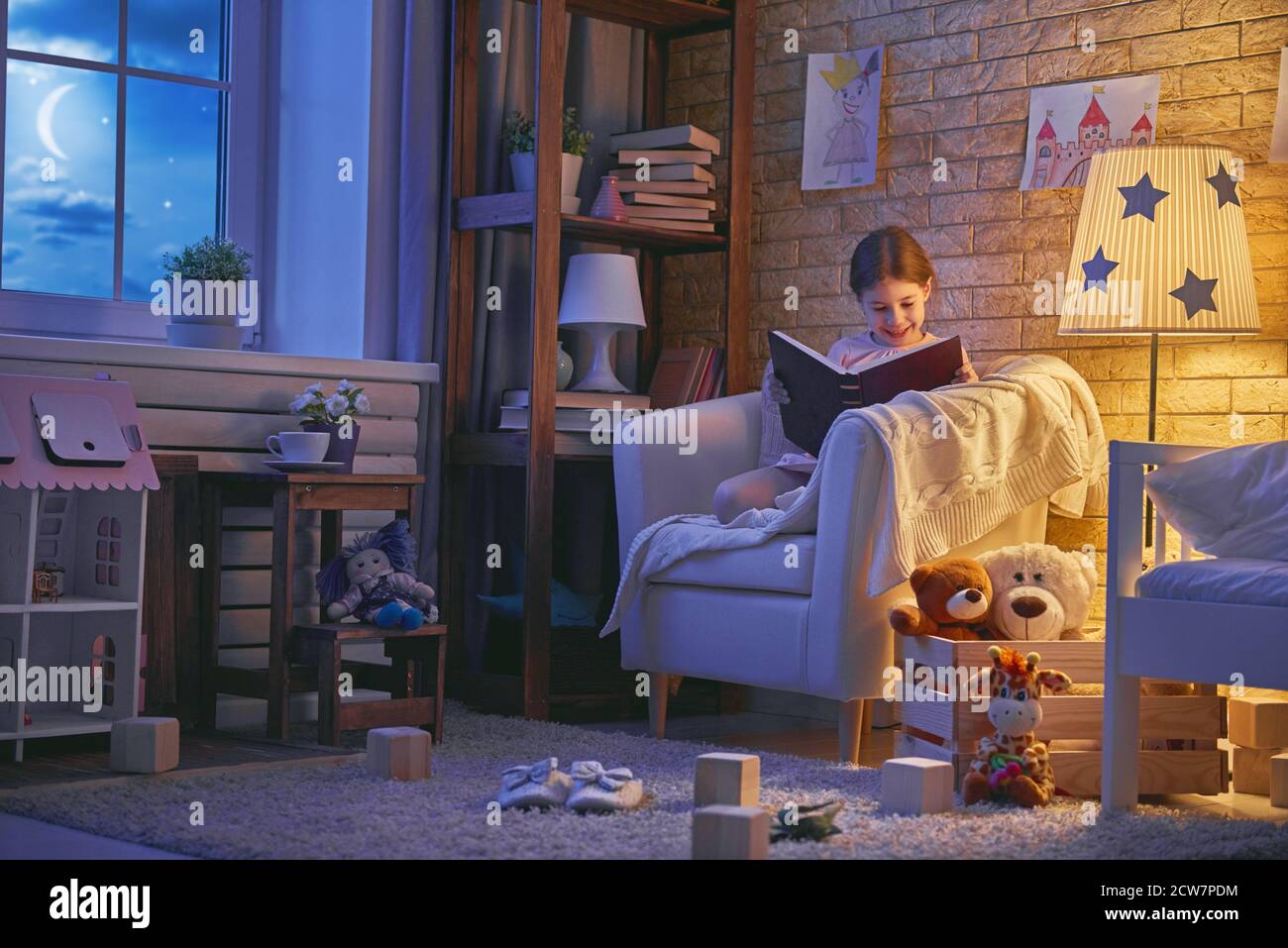 Cute little child girl reading a book under a lamp. Kid girl sitting in ...