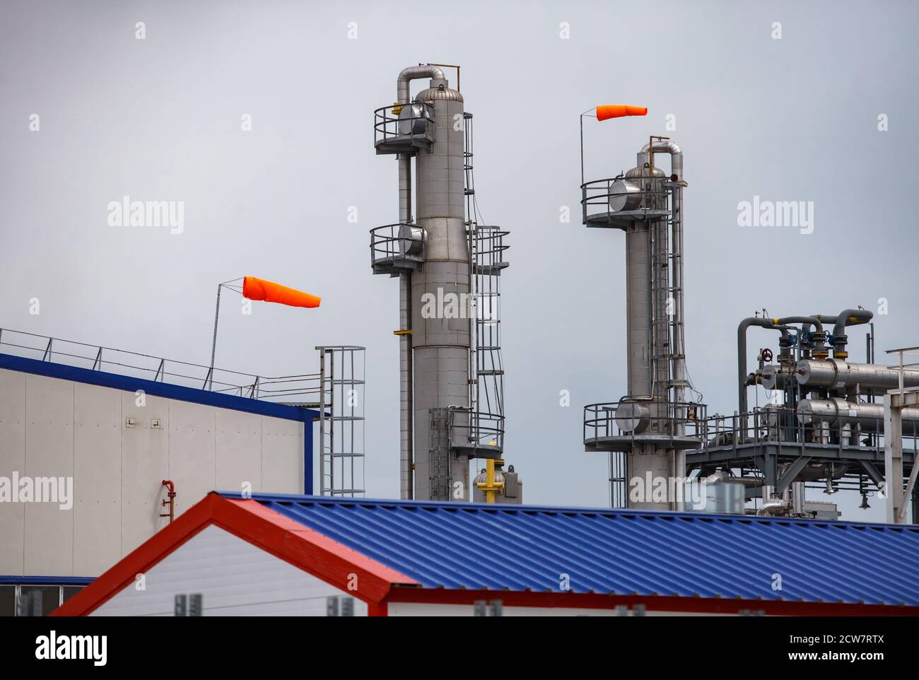 Distillation towers with orange weather vanes on grey sky background ...