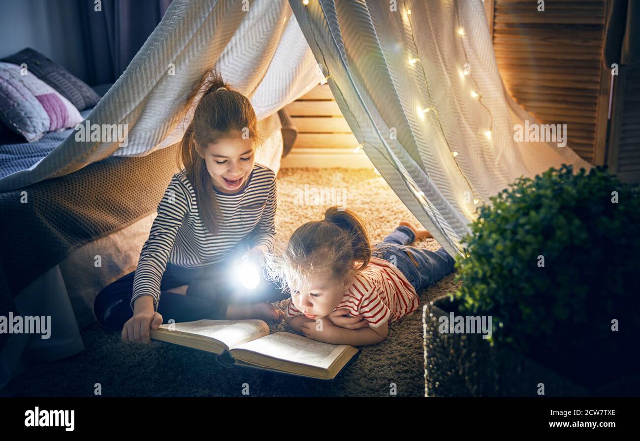 Two cute little children are reading a book with flashlights in tent ...