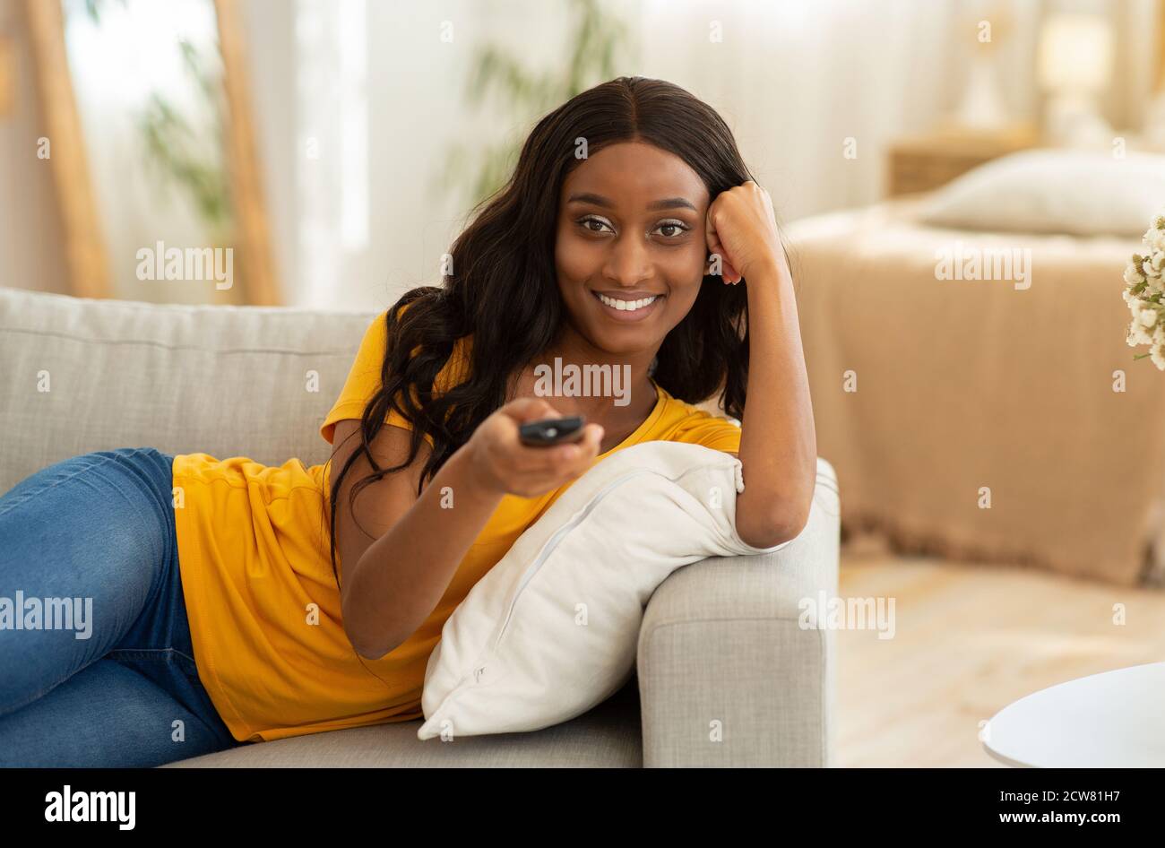 Weekend recreations. Pretty black lady with remote control watching TV ...