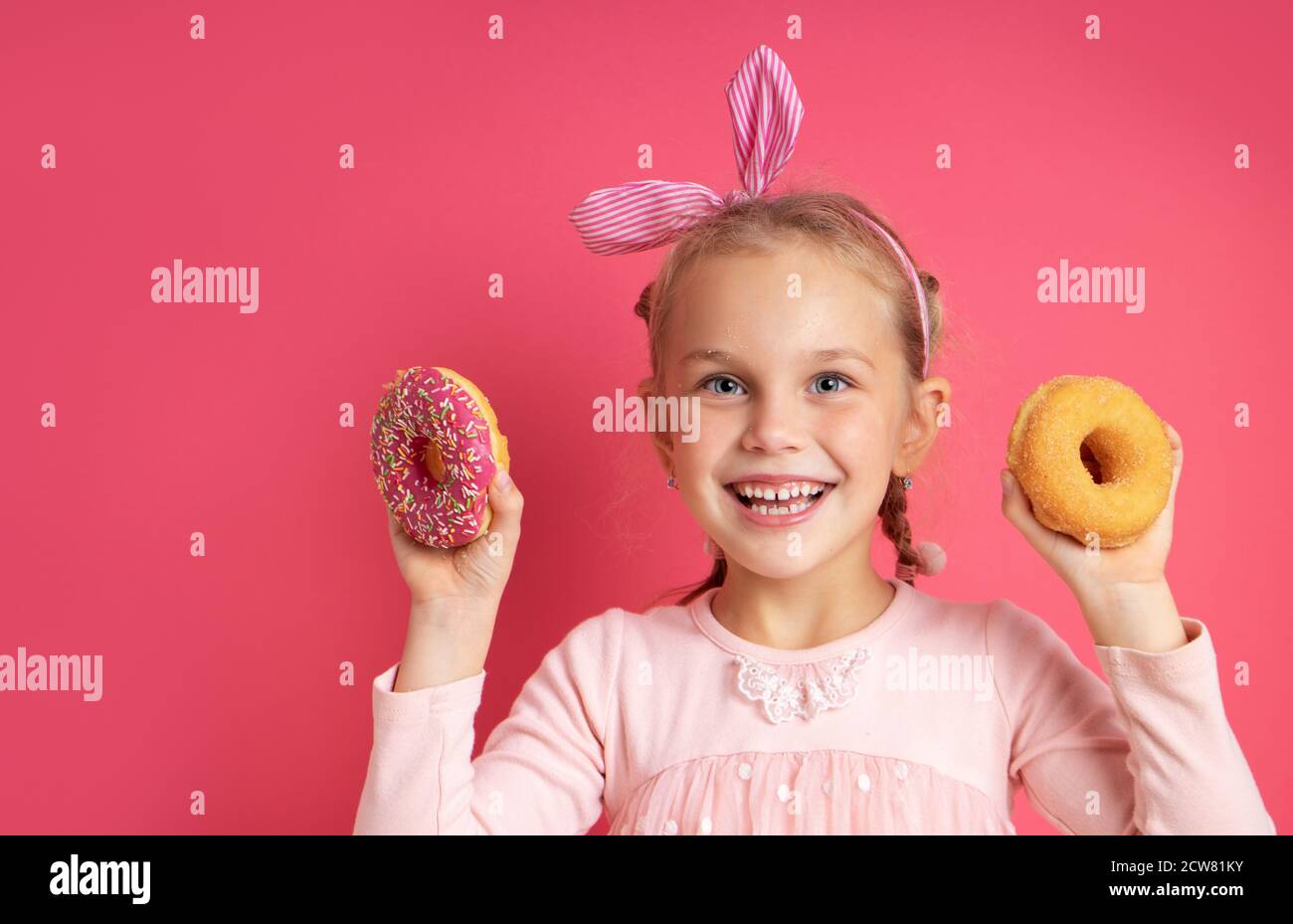Portrait cheerful little girl having fun to camera with colorful donuts ...