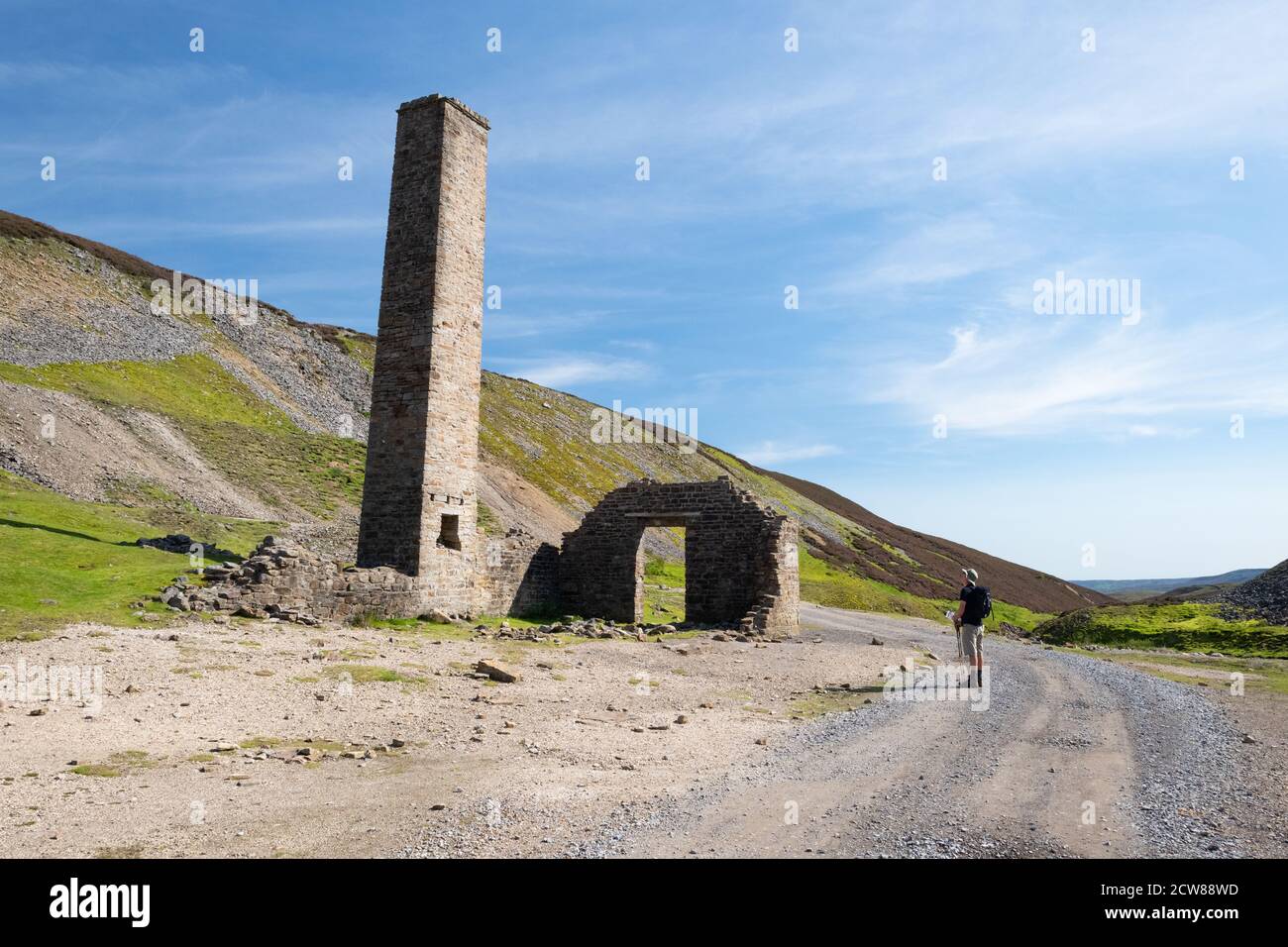 A walker on the Coast to Coast walk passing the Old Gang Smelt Mill, a ...