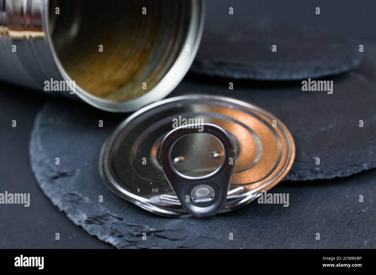 Macro closeup of isolated shiny metal food can with lid on black slate ...