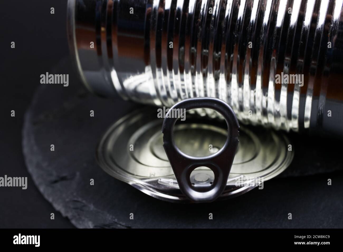 Macro closeup of isolated shiny metal food can with lid on black slate ...
