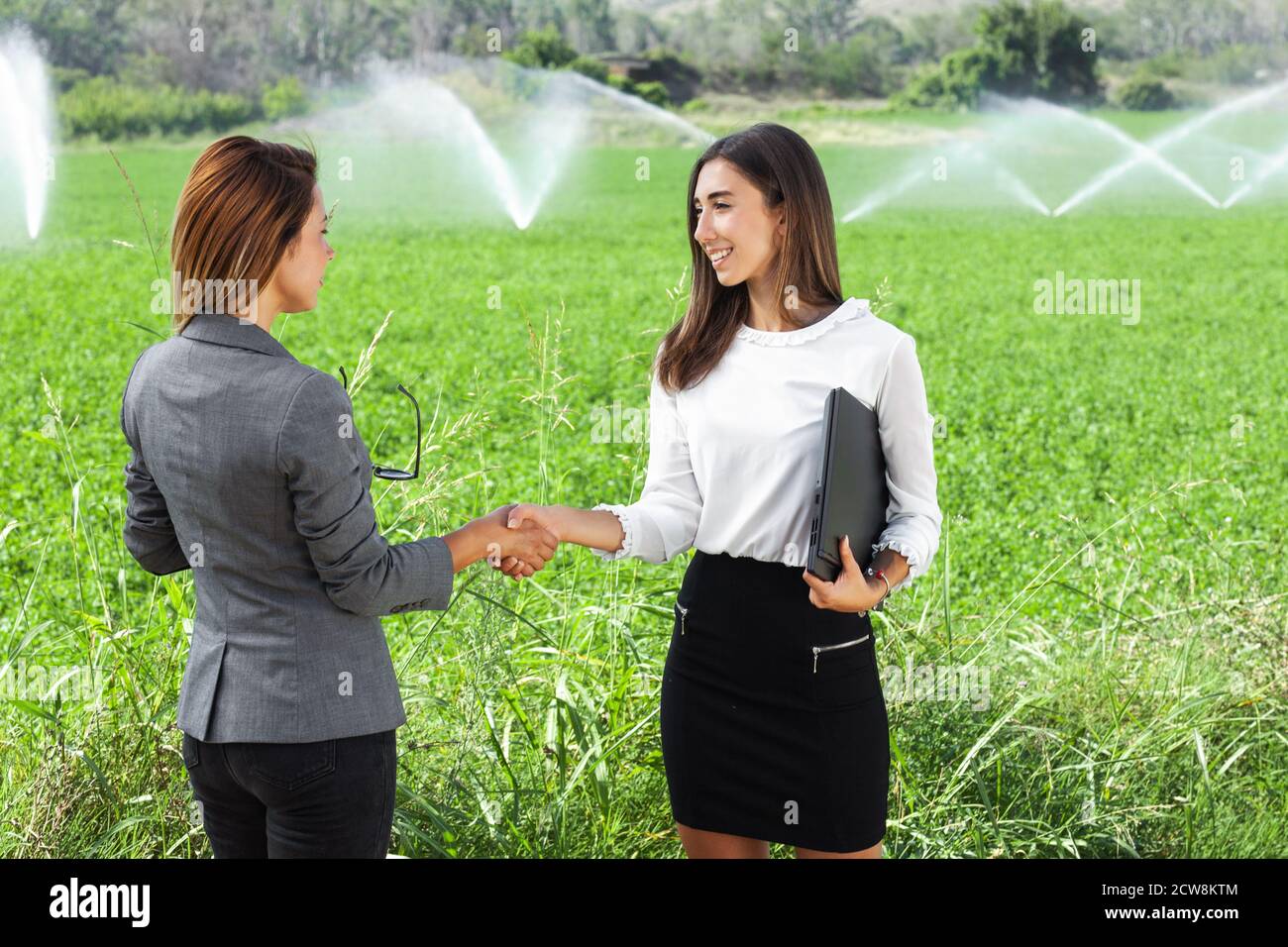 Business women shaking hands in a green field with agriculture ...