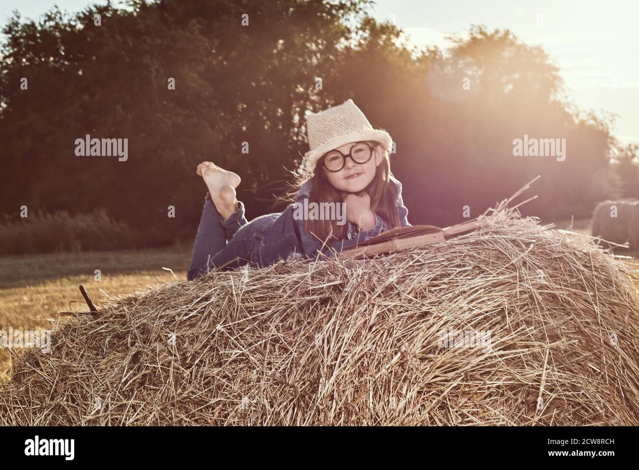 Reading girl sits over the haystack roll on field in countryside. High ...