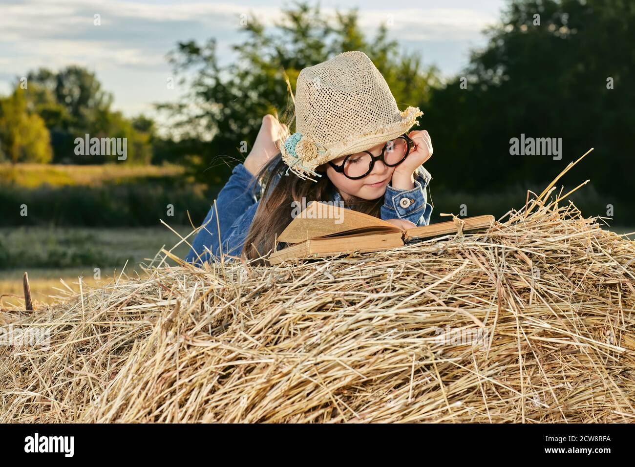 Reading girl sits over the haystack roll on field in countryside. High ...