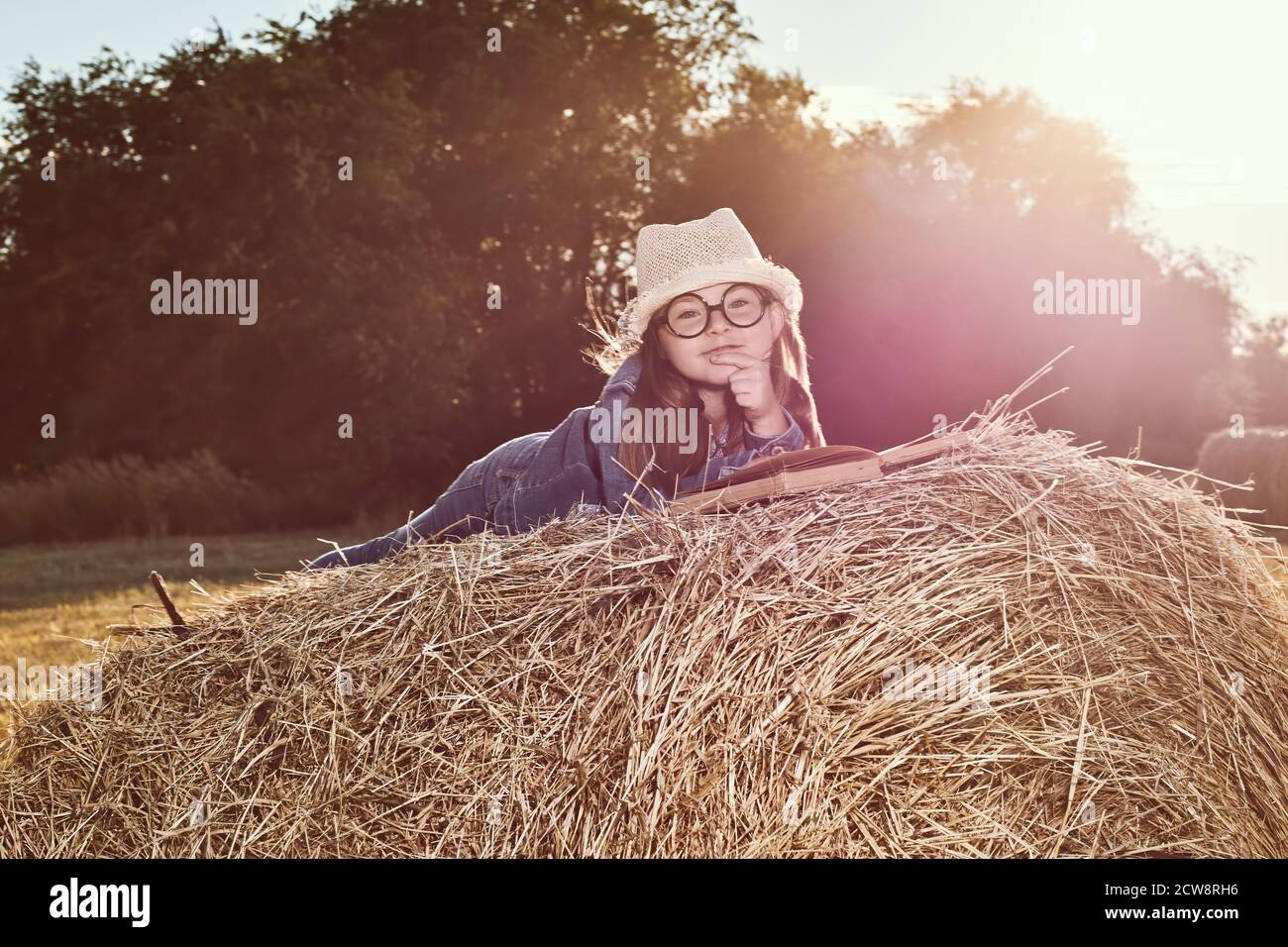 Reading girl sits over the haystack roll on field in countryside. High ...