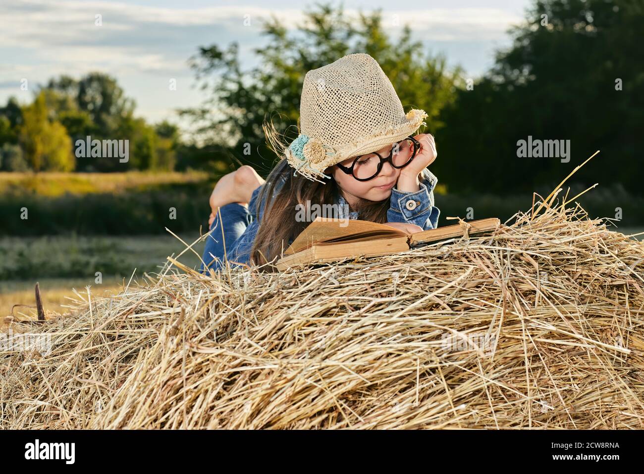 Reading girl sits over the haystack roll on field in countryside. High ...