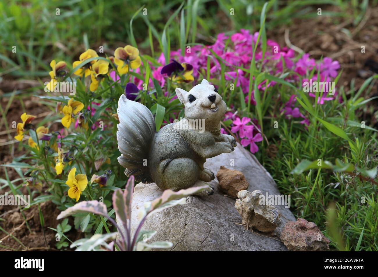 Closeup of a small squirrel statue on a rock in a garden covered in ...