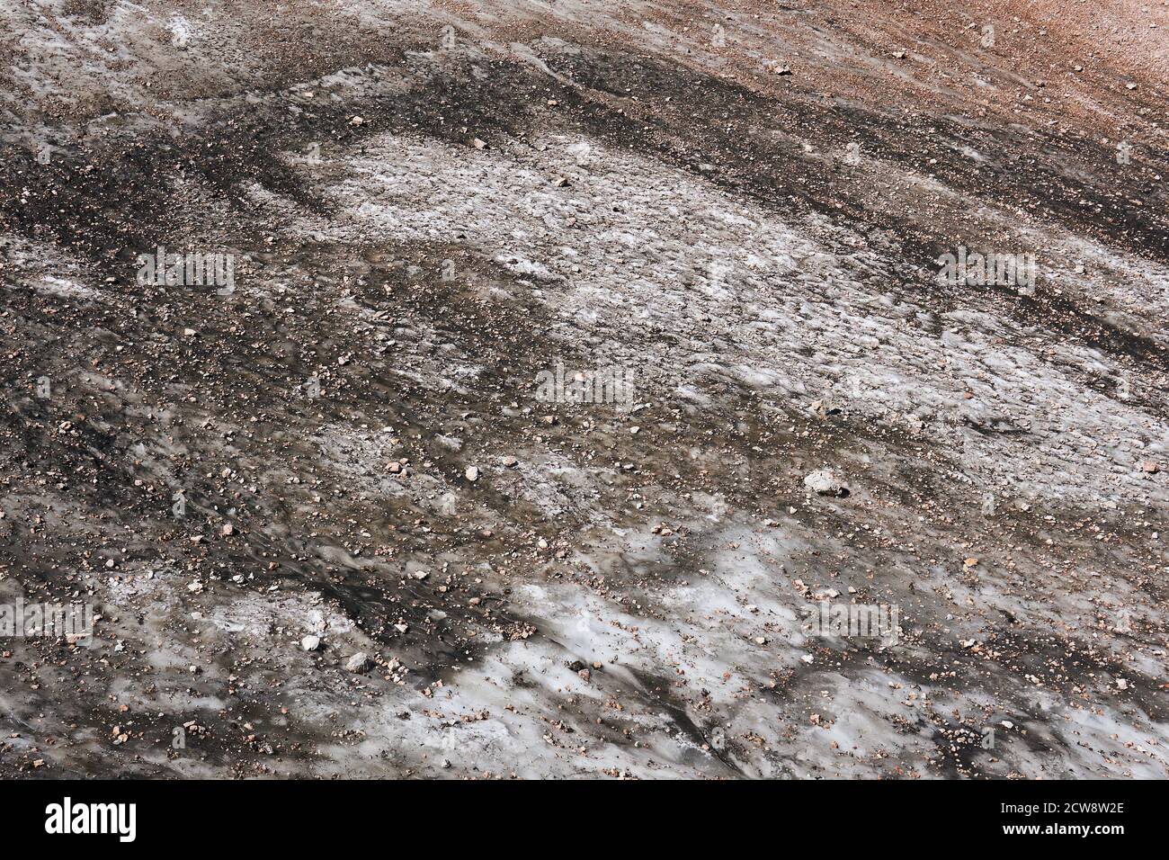 muddy surface of a melting mountain glacier covered with rocks and ...