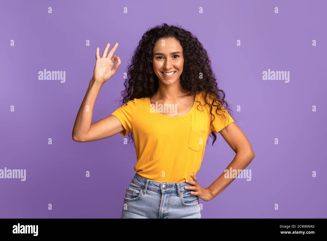 It's OK. Cheerful young brunette woman gesturing okay sign over purple ...