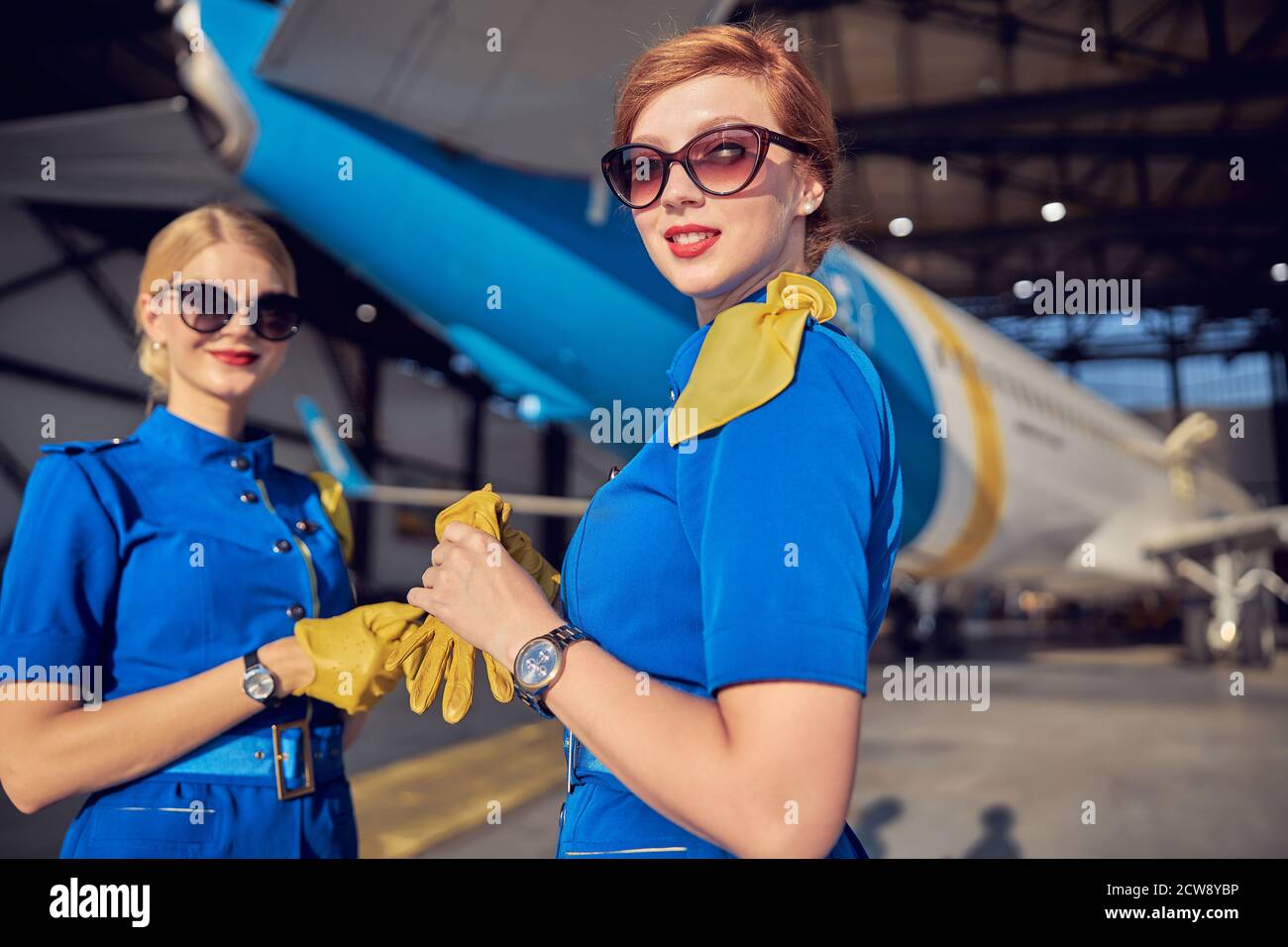 Happy smiling two flight attendant in uniform and leather gloves posing ...