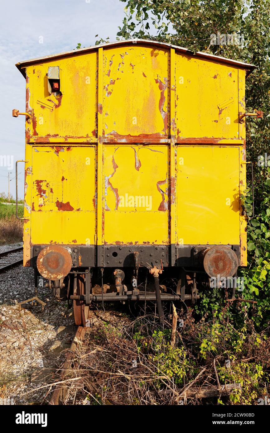Back view of an old yellow train, abandoned and rusty, on an old tracks ...