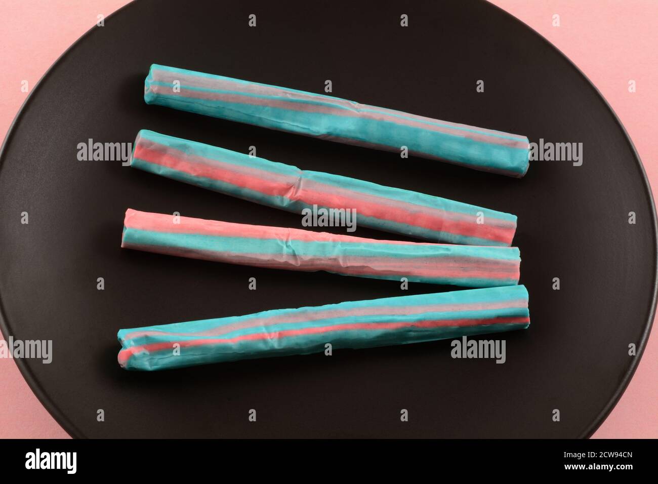 Strawberry milkshake chew candy sticks on black snack plate on pink ...
