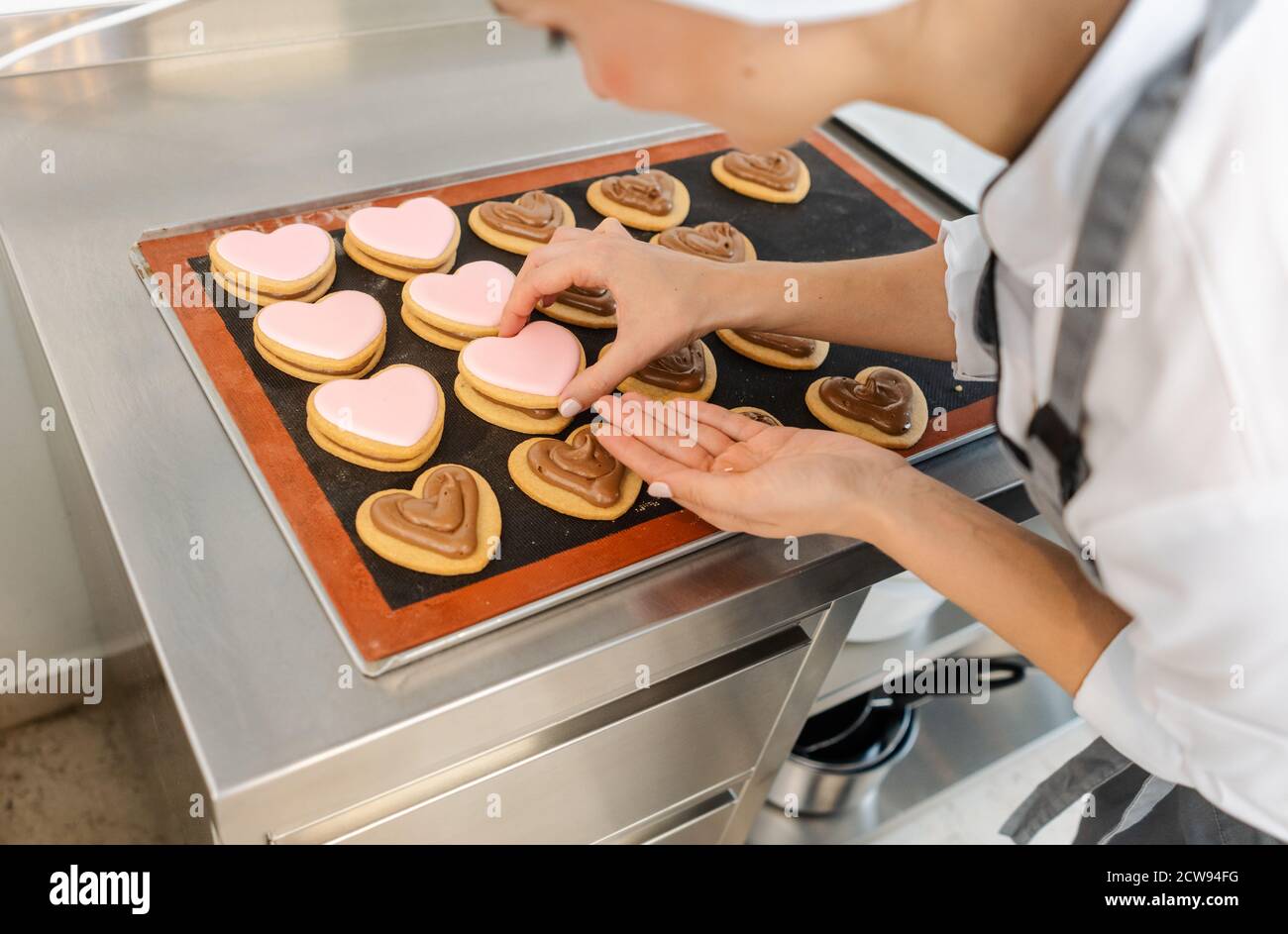 Confectioner woman using pastry bag to put cream on top of cookies ...