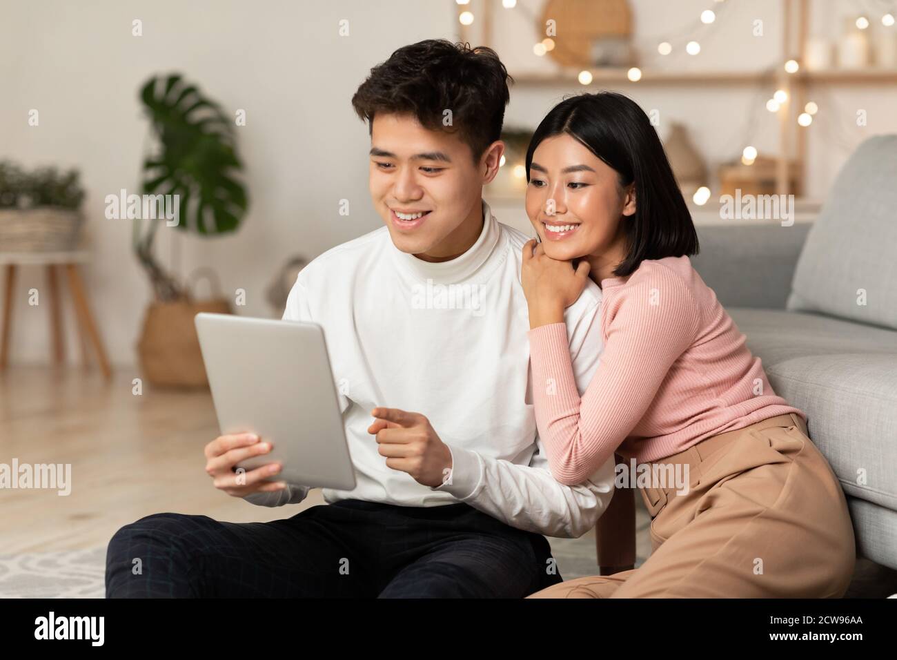 Happy Korean Couple Using Tablet Computer Sitting At Home Stock Photo ...