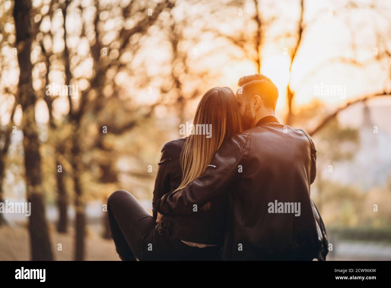 A romantic couple sitting on a bench hugging and watching the sunset in ...