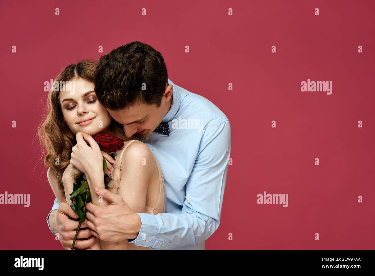enamored man and woman with a red flower on a pink background hug each ...