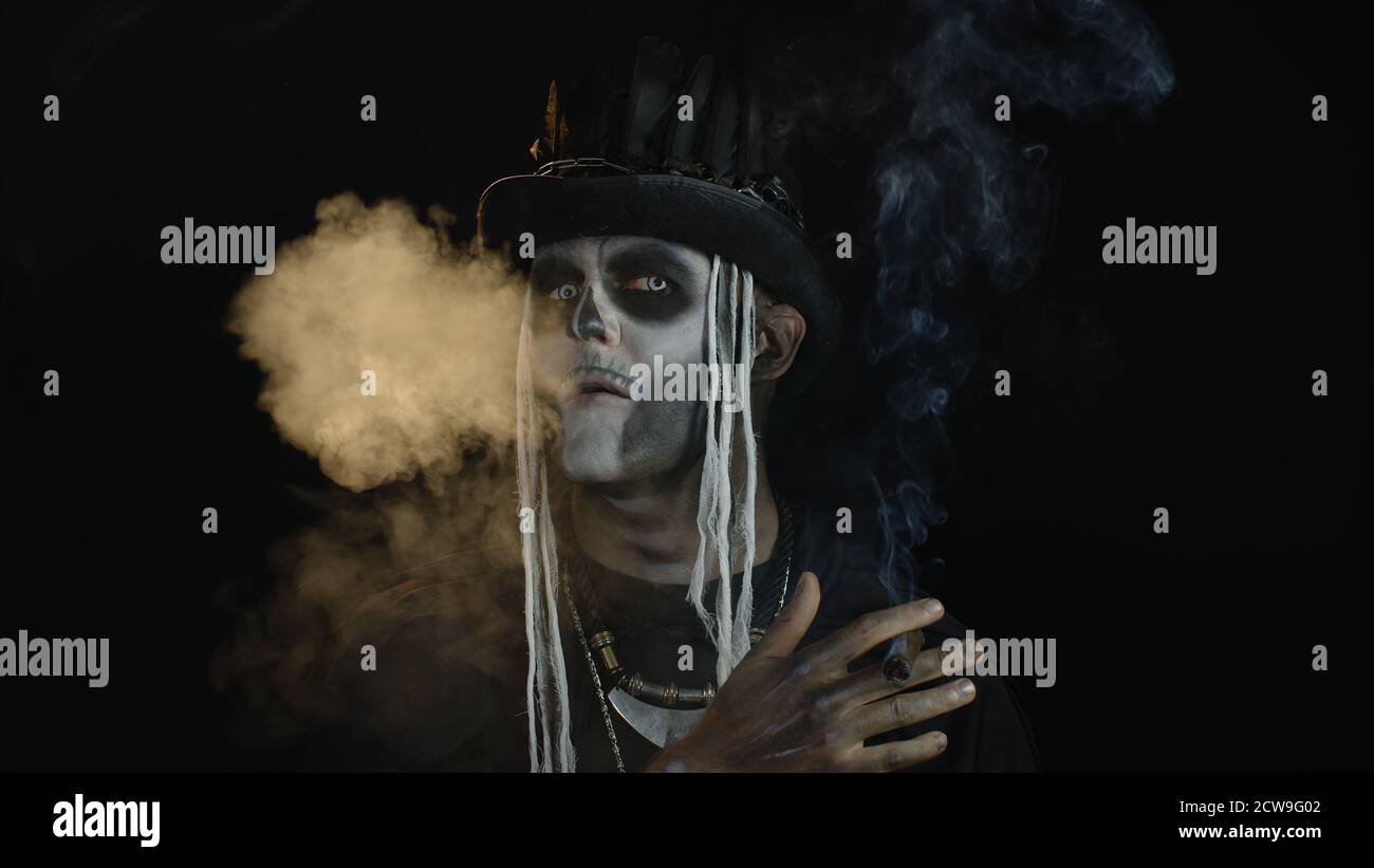 Creepy man with skeleton makeup in top-hat with feathers. Guy smoking ...