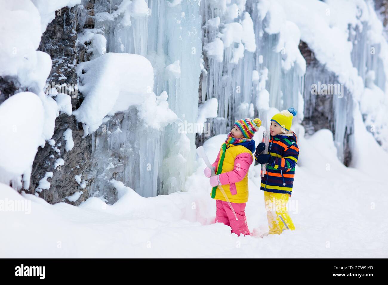 Children play with icicle in snow. Kids lick icicles at frozen mountain ...