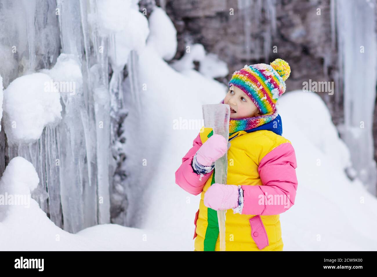 Children play with icicle in snow. Kids lick icicles at frozen mountain ...