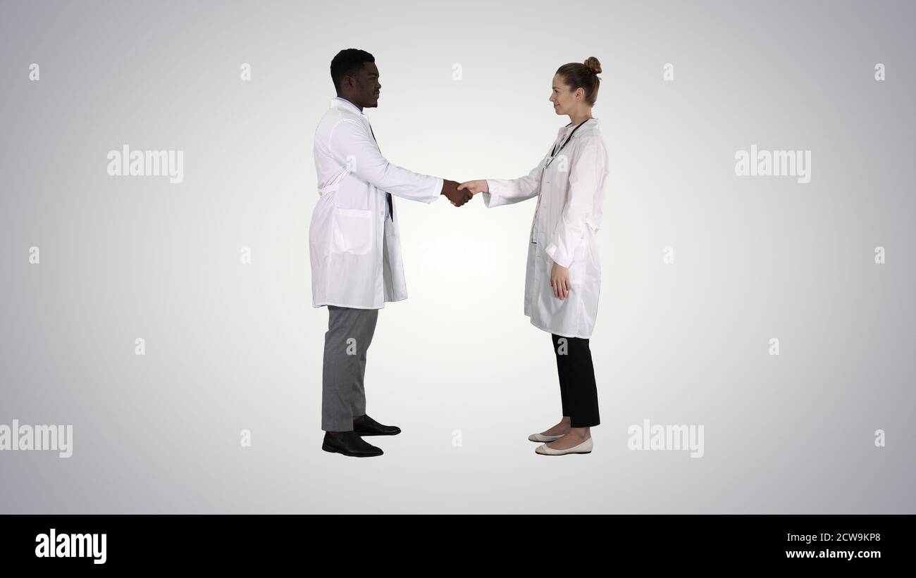 Two young doctor shaking hands on gradient background Stock Photo - Alamy