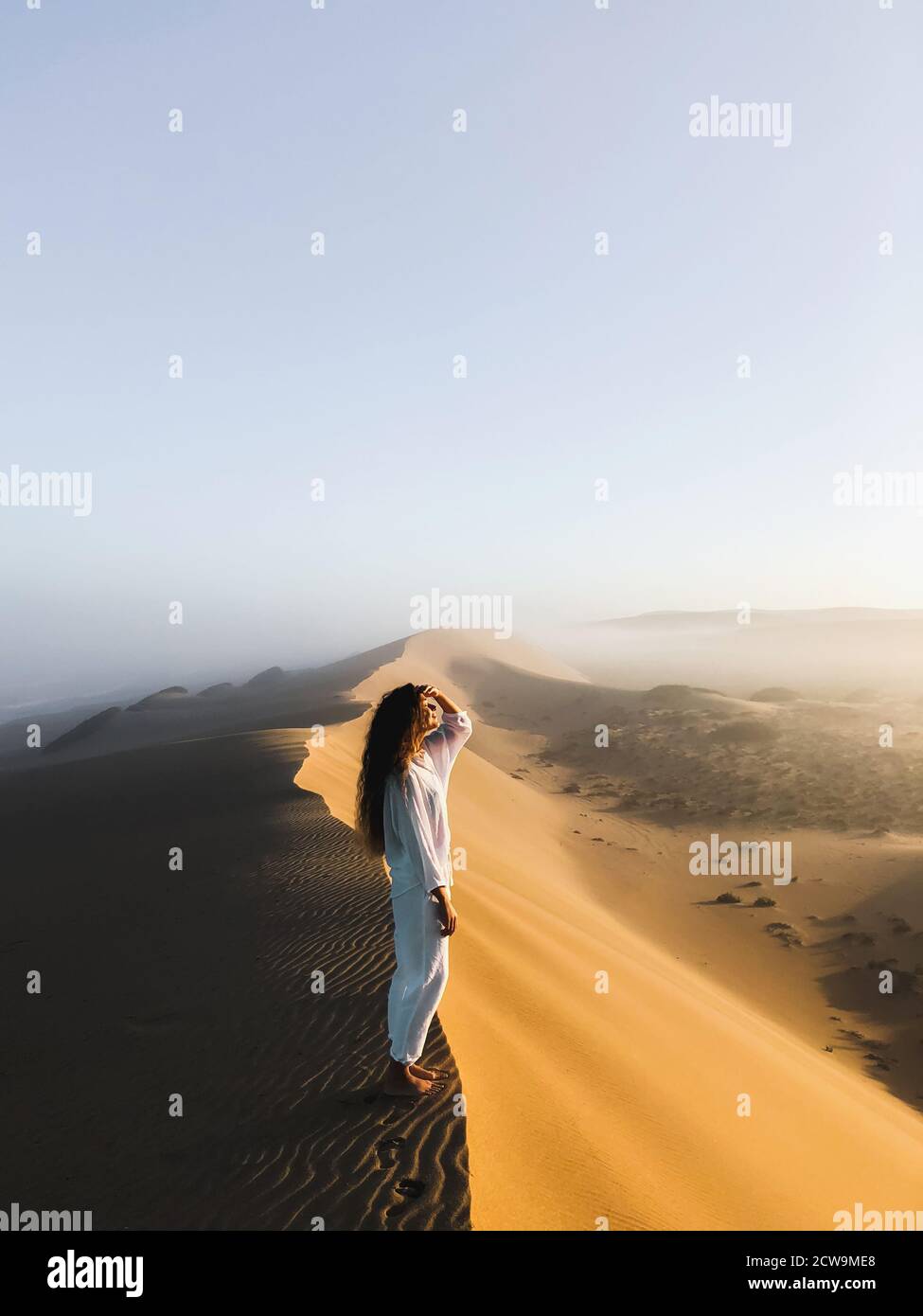 Woman enjoying sunrise on top of huge sand dune. Beautiful warm sun ...