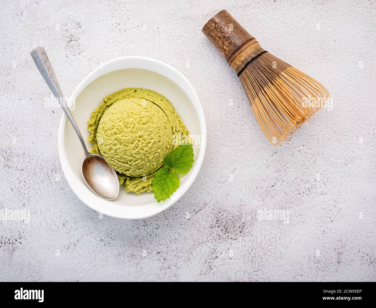 Matcha green tea ice cream with matcha whisk brush setup on white stone ...