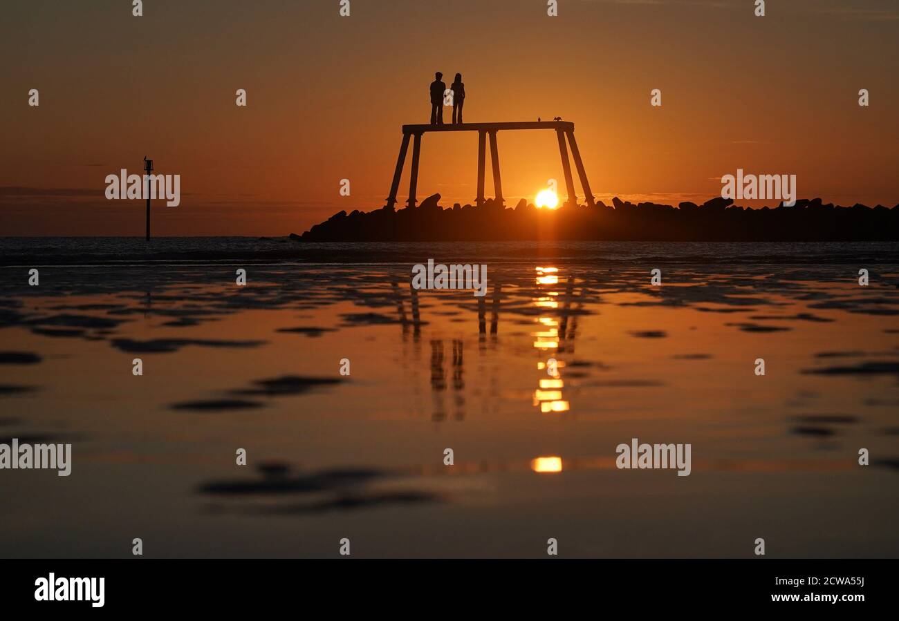 The sun rises behind Sean Henry's The Couple Statue at Newbiggin-by-the ...