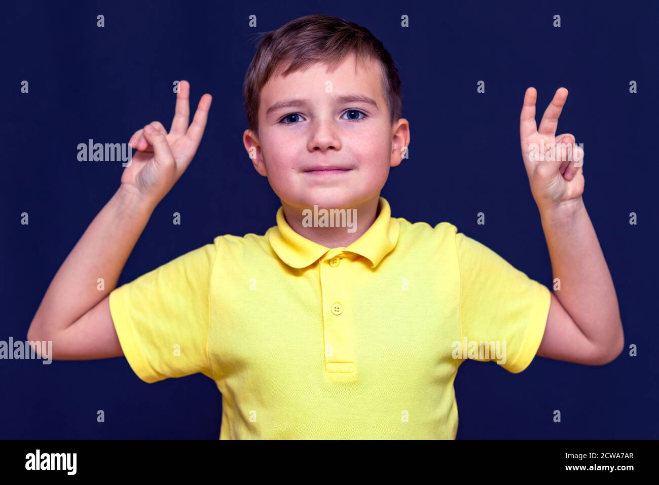 boy with fingers shows peace or victory sign on blue dark studio ...