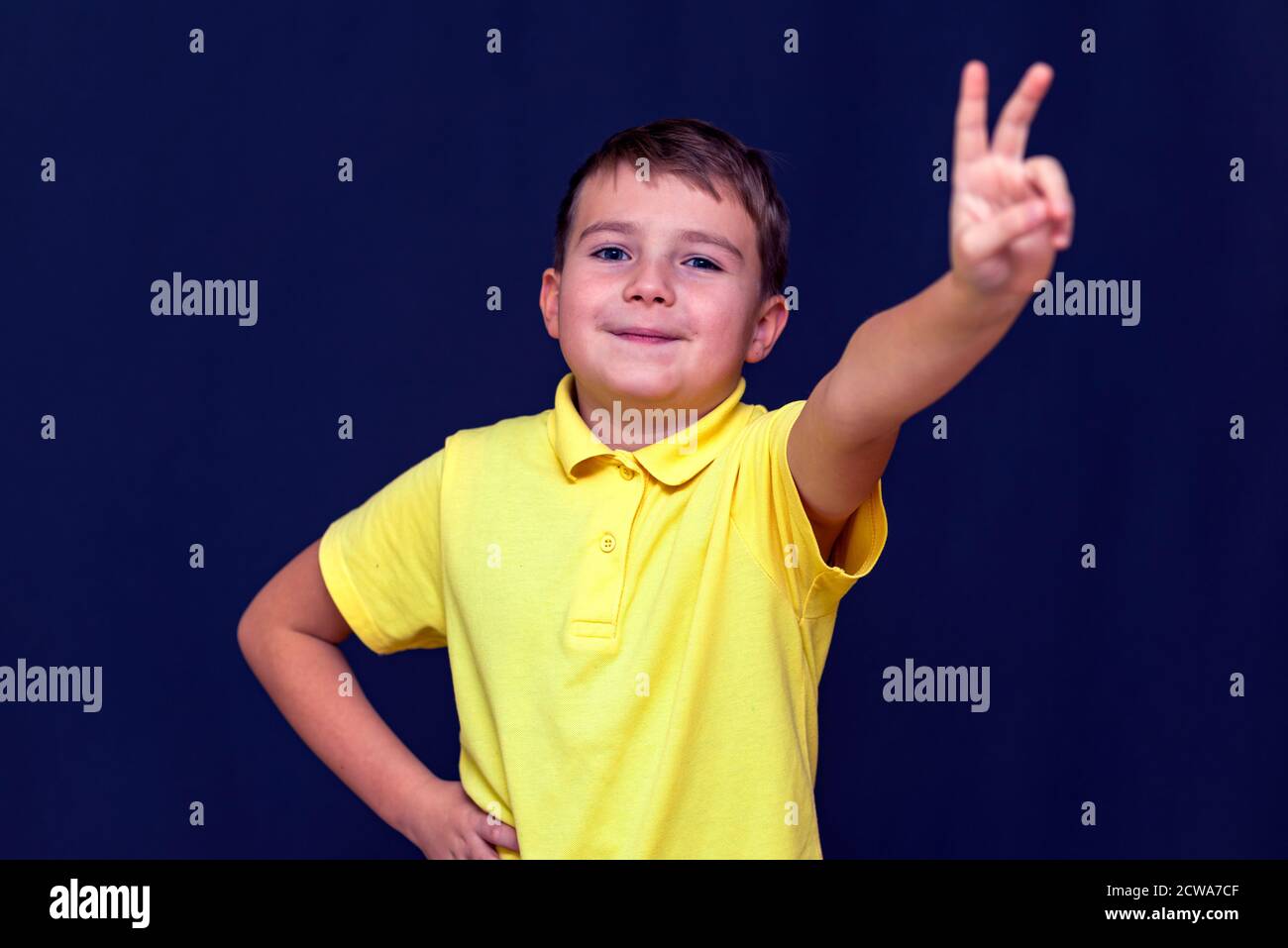boy with fingers shows peace or victory sign on blue dark studio ...