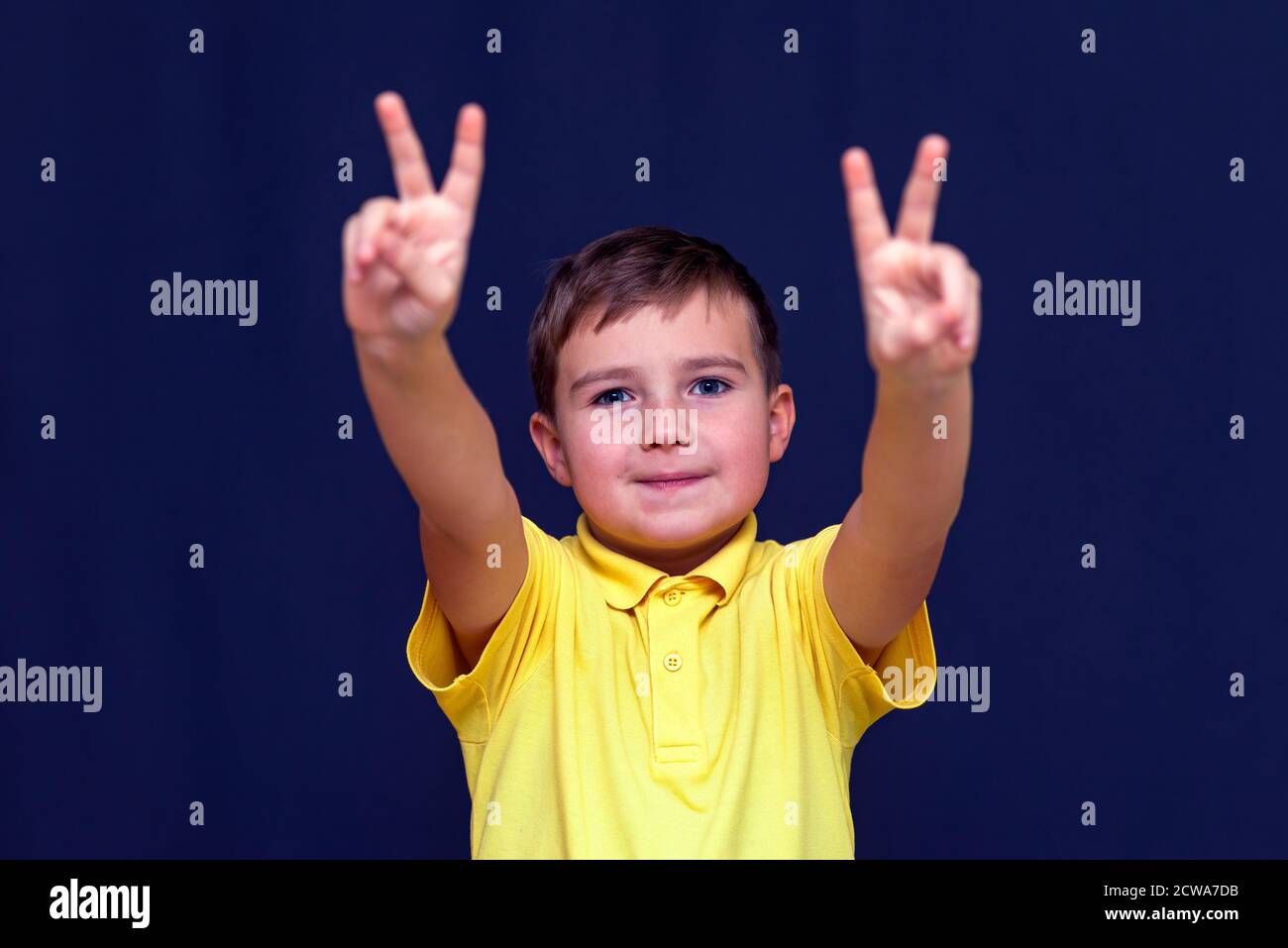boy with fingers shows peace or victory sign on blue dark studio ...
