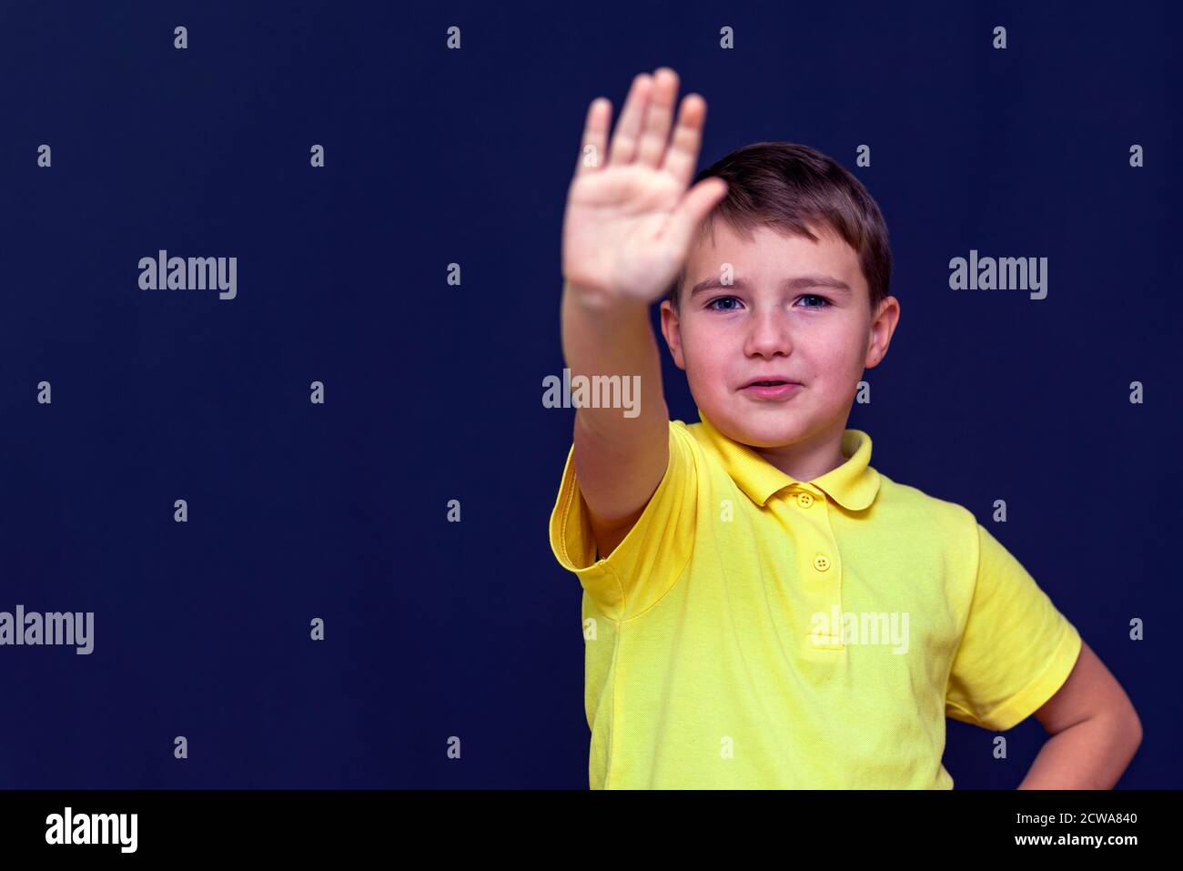 Little 9s boy putting his hand out making stop sign gesture.Blue studio ...