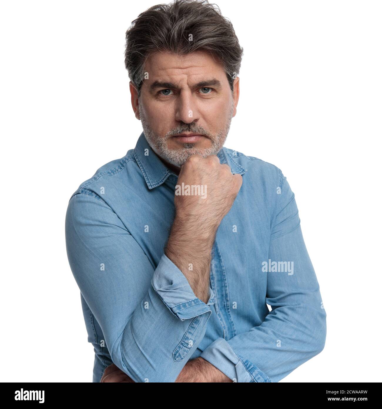 Angry casual man looking forward and frowning with his hand on his chin ...