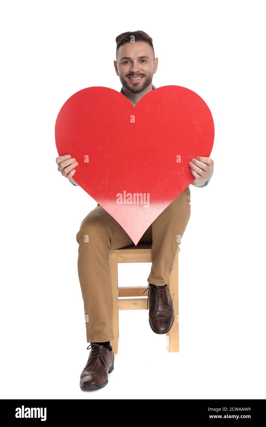 happy casual man smling and holding big red heart, sitting isolated on ...