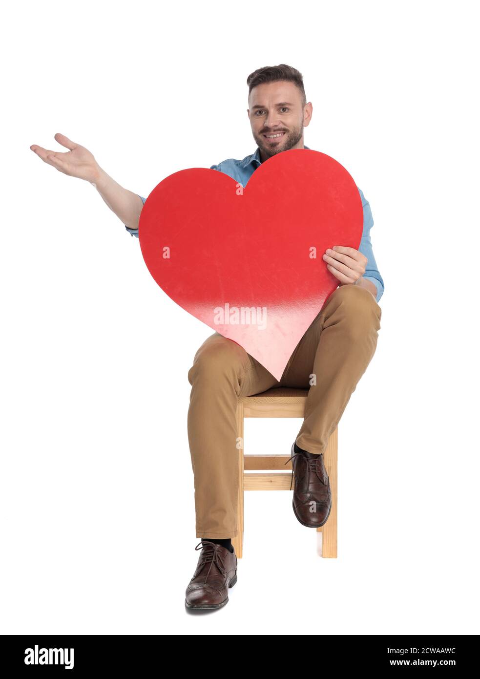 happy casual man holding big red heart and presenting to side, sitting ...