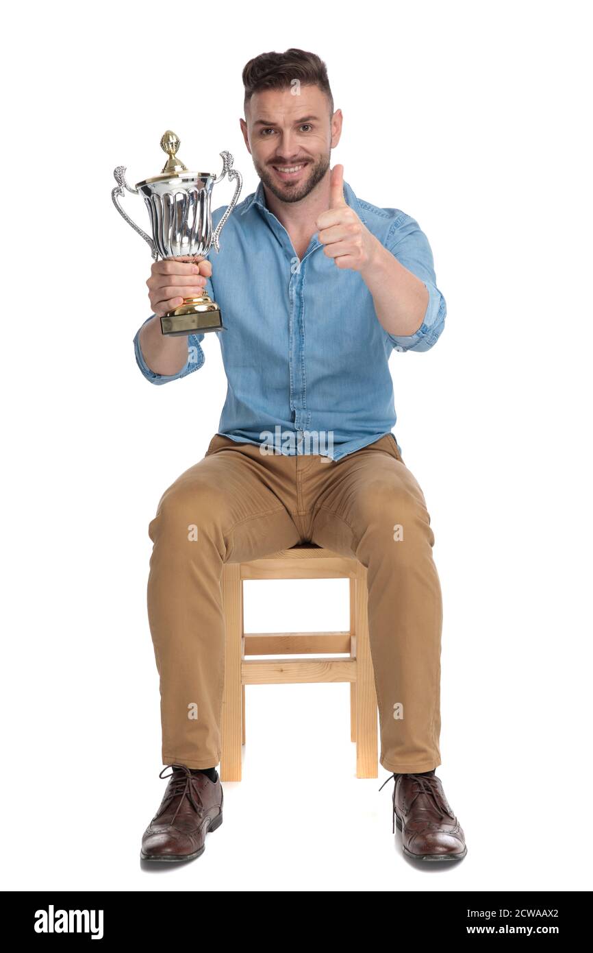 happy young casual man holding trophy and making thumbs up sign ...