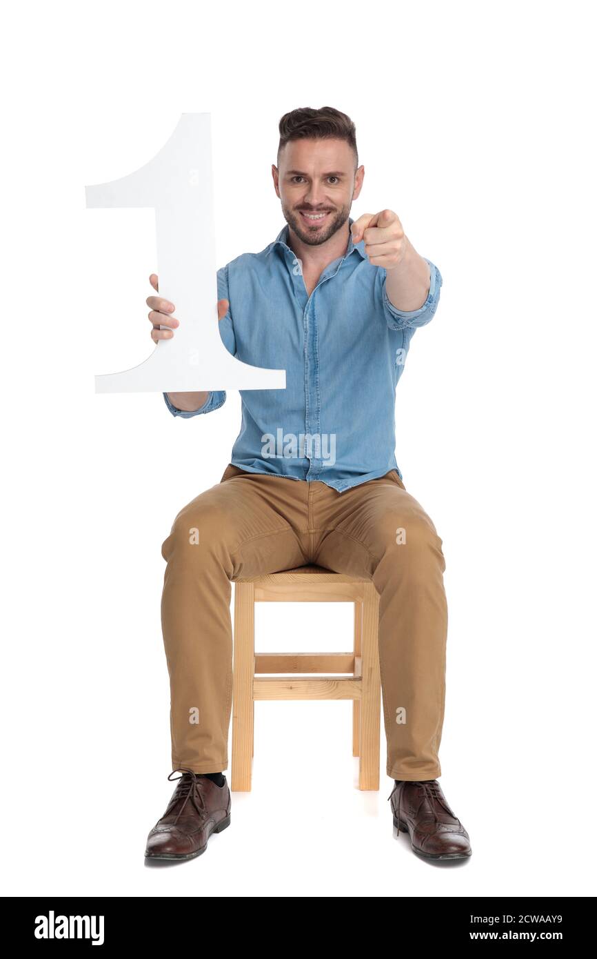 happy young man holding number one sign and pointing finger, sitting ...