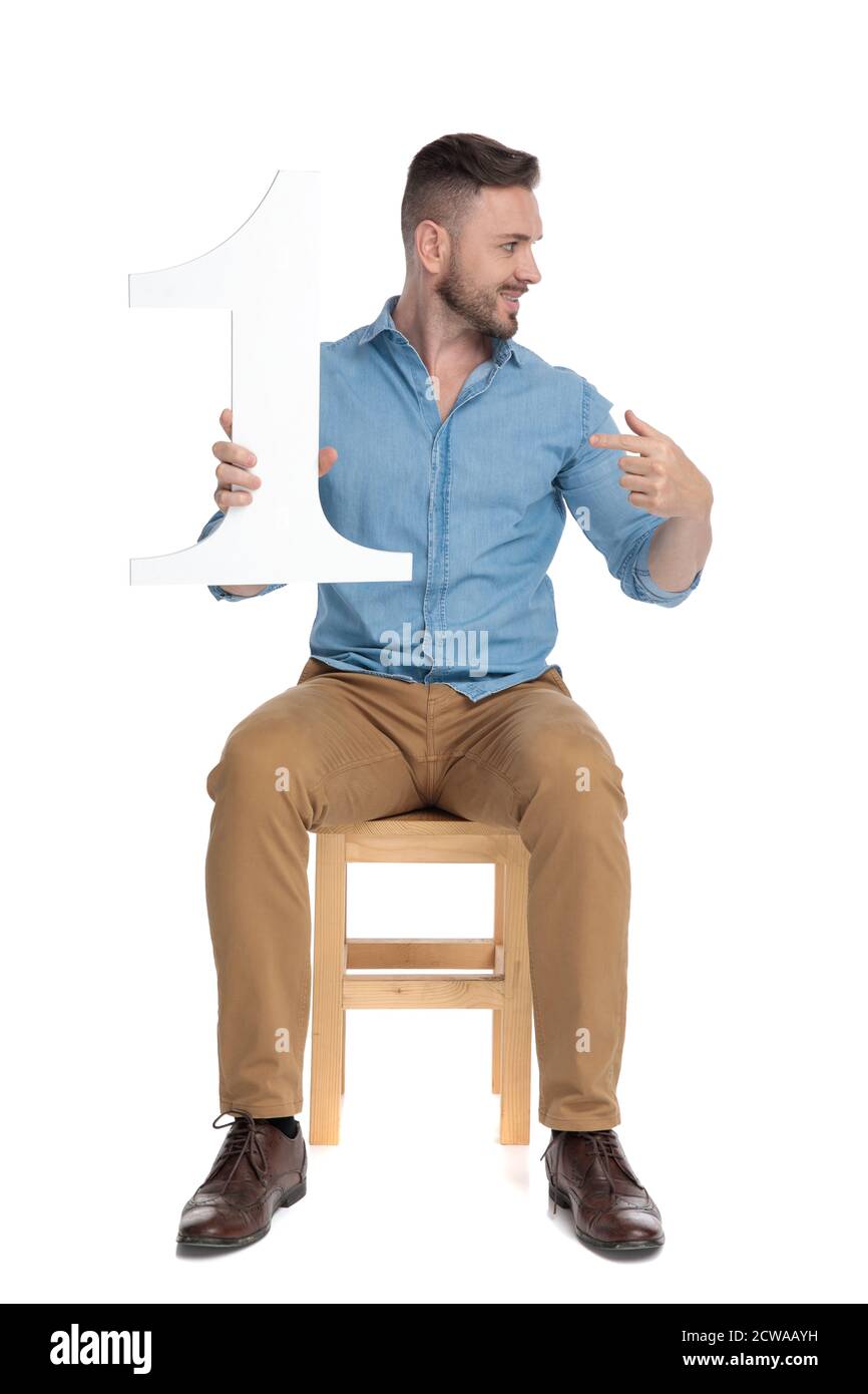 young casual man holding number one sign and presenting to side ...