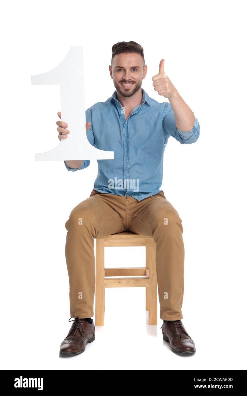 young casual guy holding number one sign and making thumbs up sign ...